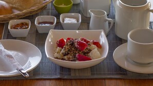 Mesa posta para o pequeno-almoço com iogurte, morangos, granola, chávena de café e diversos acompanhamentos.