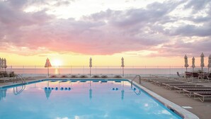 Piscina com espreguiçadeiras e guarda-sóis, cerca e vista para o pôr do sol.
