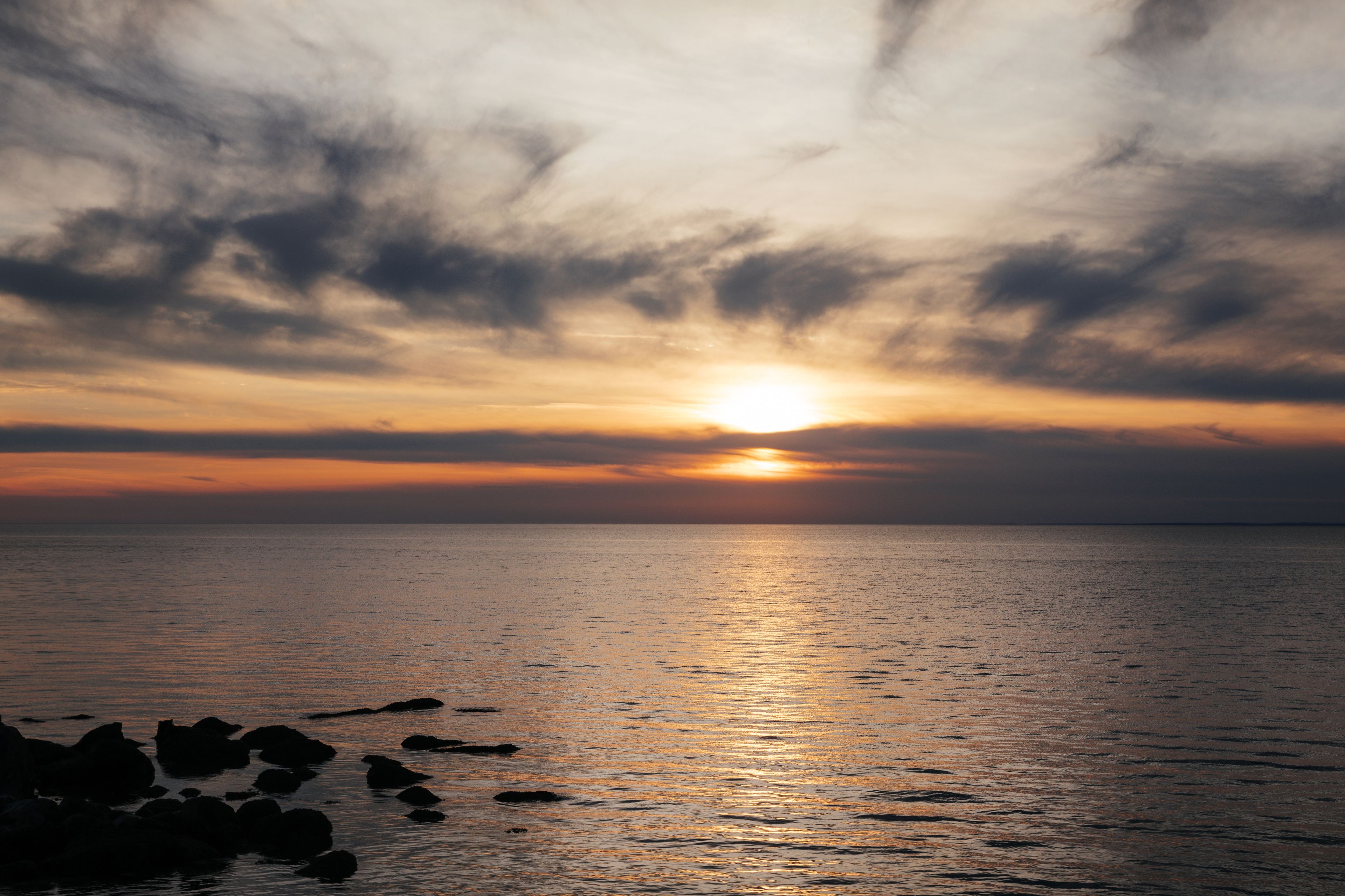 Um pôr do sol sobre um mar calmo, com pedras em primeiro plano.