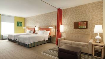 Quarto de hotel com duas camas, um sofá, uma mesinha e um abajur.
