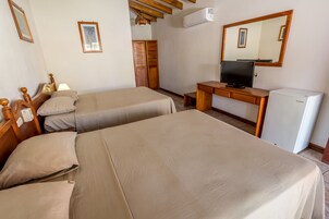Quarto de hotel com duas camas, uma escrivaninha com computador, televisão e mini-geladeira.