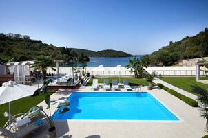 Piscina com espreguiçadeiras, vista para o mar e um morro.