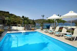 Piscina com espreguiçadeiras e guarda-sóis, rodeada por vegetação e vista para o mar.