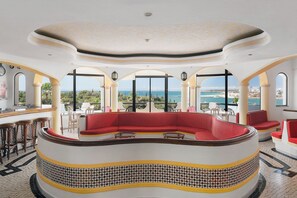 Uma área de estar circular com um banco curvo, um bar e vista para o mar.