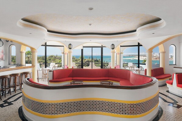 Uma área de estar circular com um banco curvo, um bar e vista para o mar.