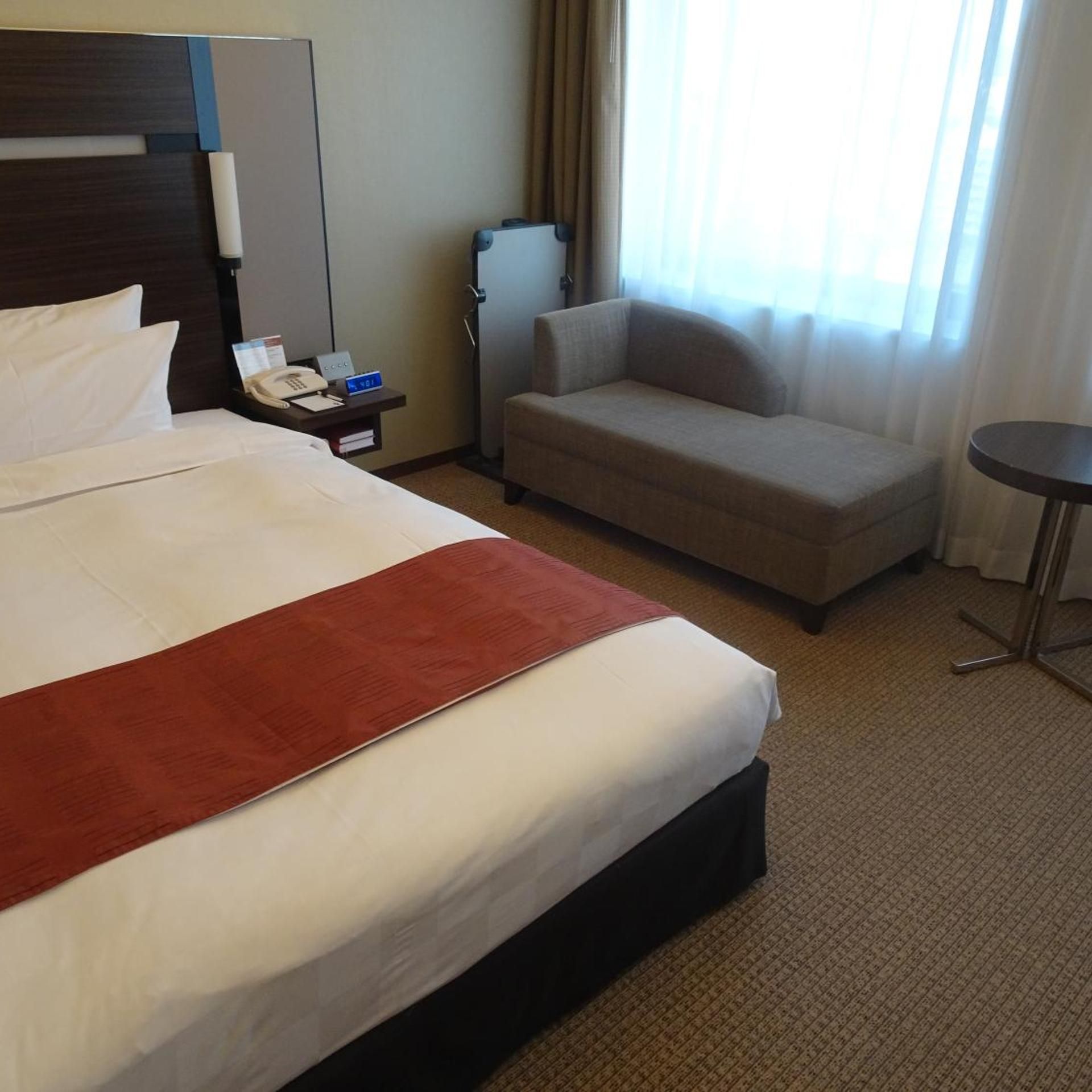 Quarto de hotel com cama grande, sofá, escrivaninha com telefone e janela com cortinas.