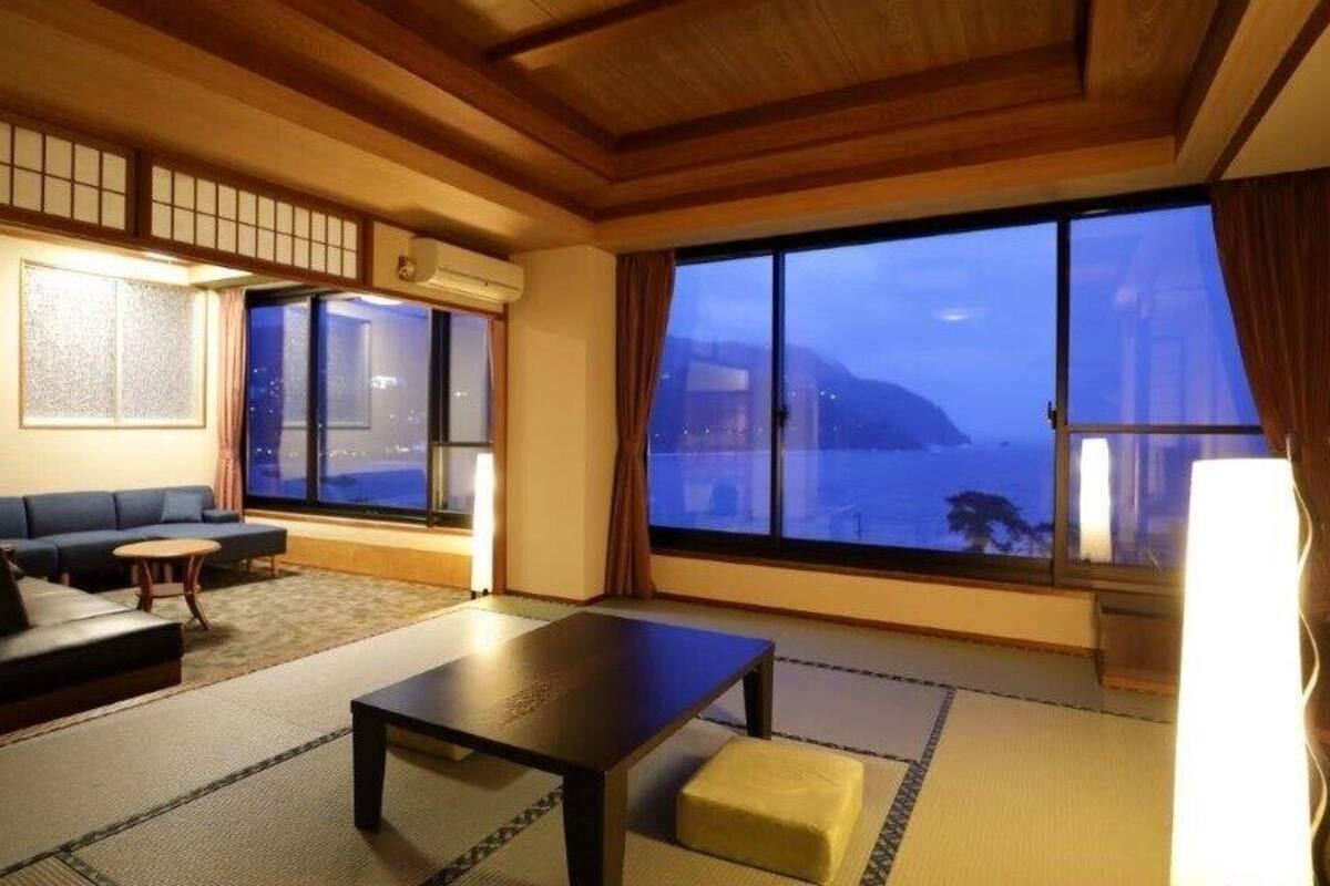 Um quarto japonês tradicional com tatames, um sofá, uma mesa e uma grande janela com vista para o mar.