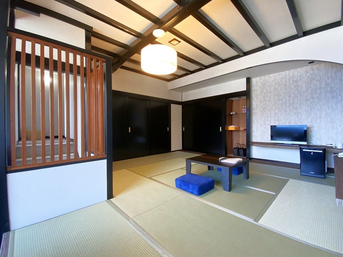 Um quarto com esteiras de tatame, uma televisão, uma escrivaninha e uma porta tradicional japonesa de correr.