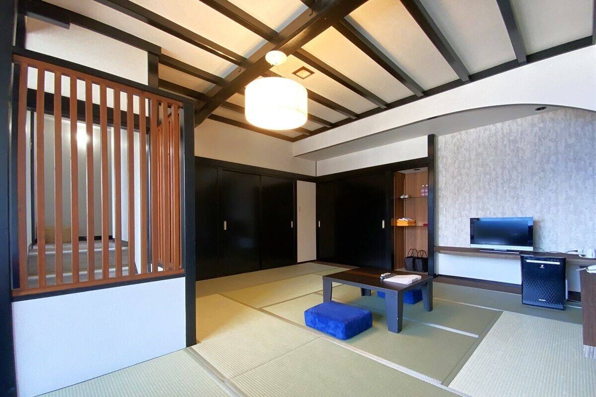 Um quarto com esteiras de tatame, uma televisão, uma escrivaninha e uma porta tradicional japonesa de correr.