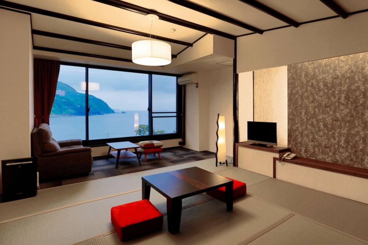 Quarto de hotel moderno com uma janela grande, um sofá, uma mesa e uma televisão.