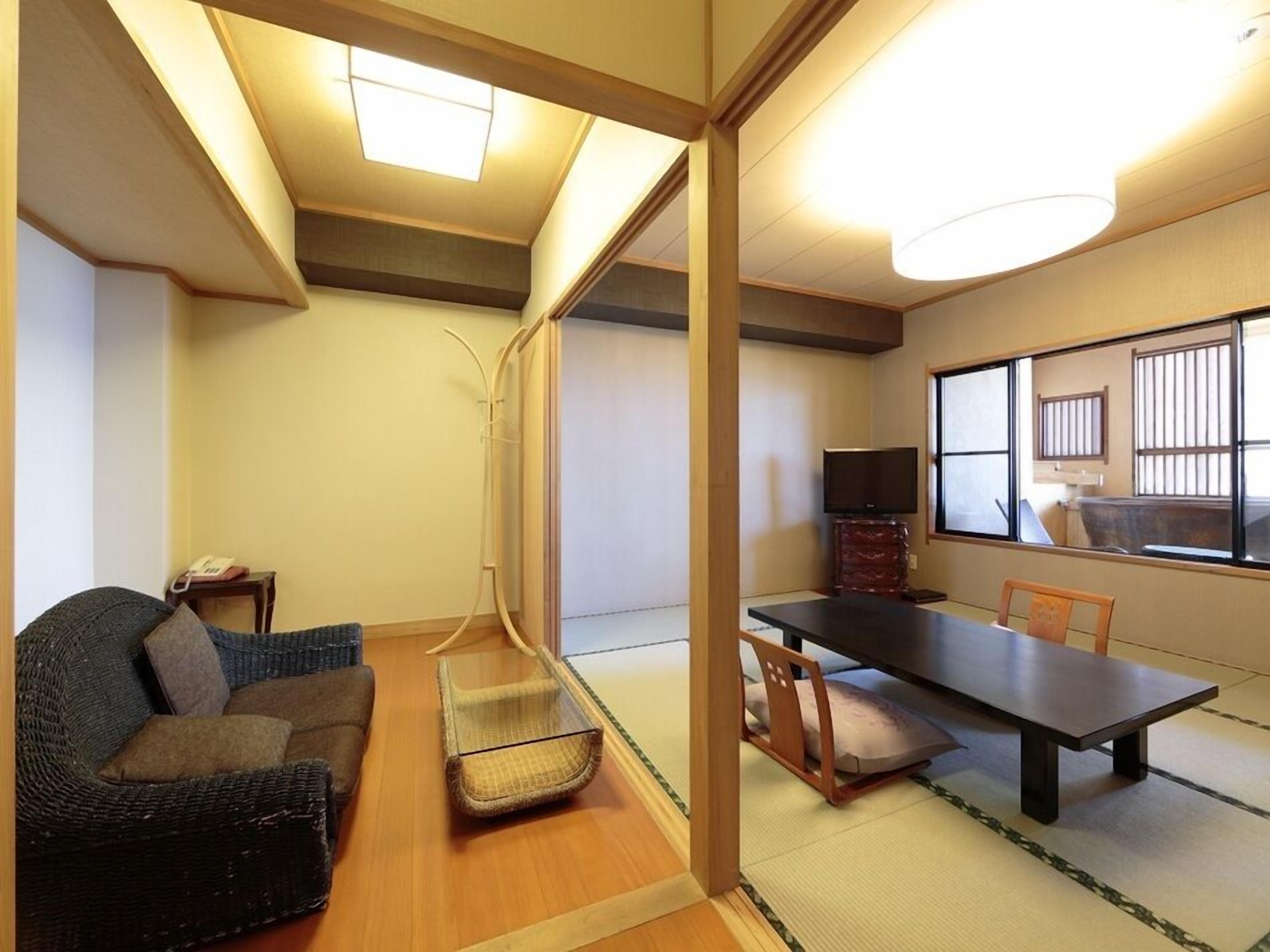 Um quarto japonês tradicional com tatames, uma mesa baixa, um sofá, uma televisão e uma porta deslizante.