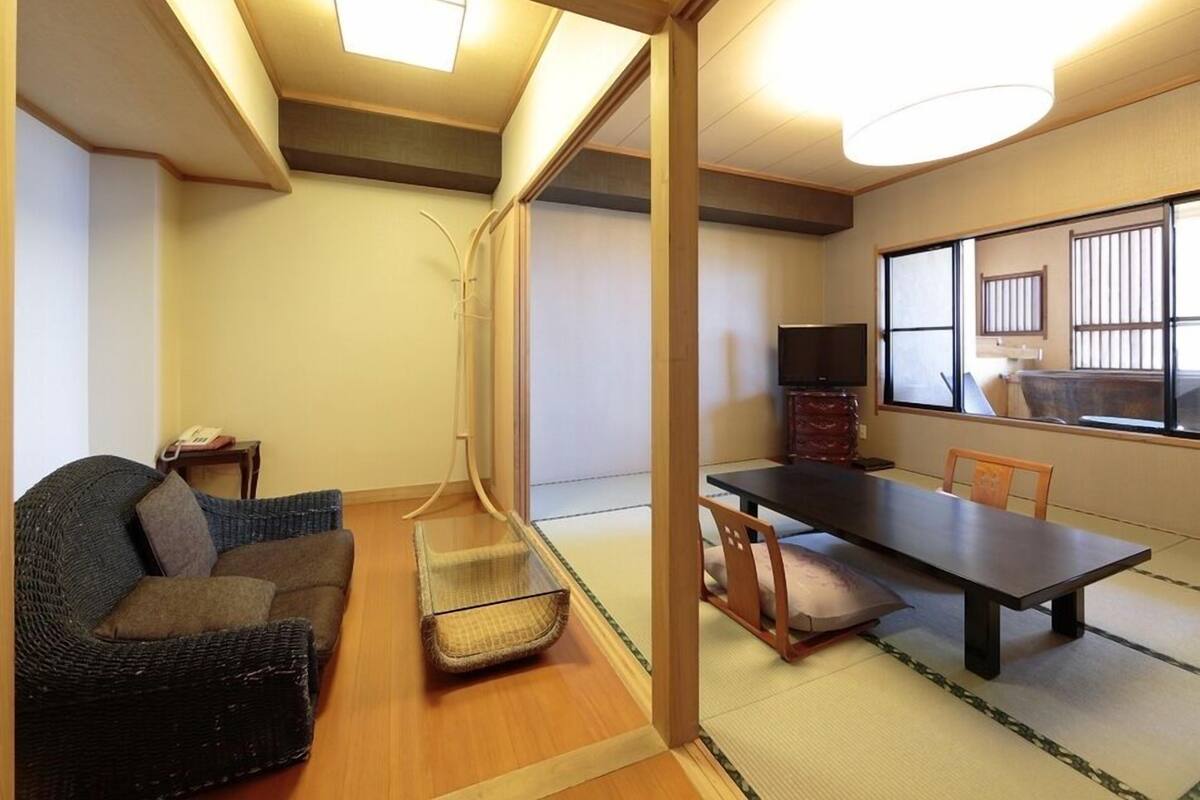Um quarto japonês tradicional com tatames, uma mesa baixa, um sofá, uma televisão e uma porta deslizante.