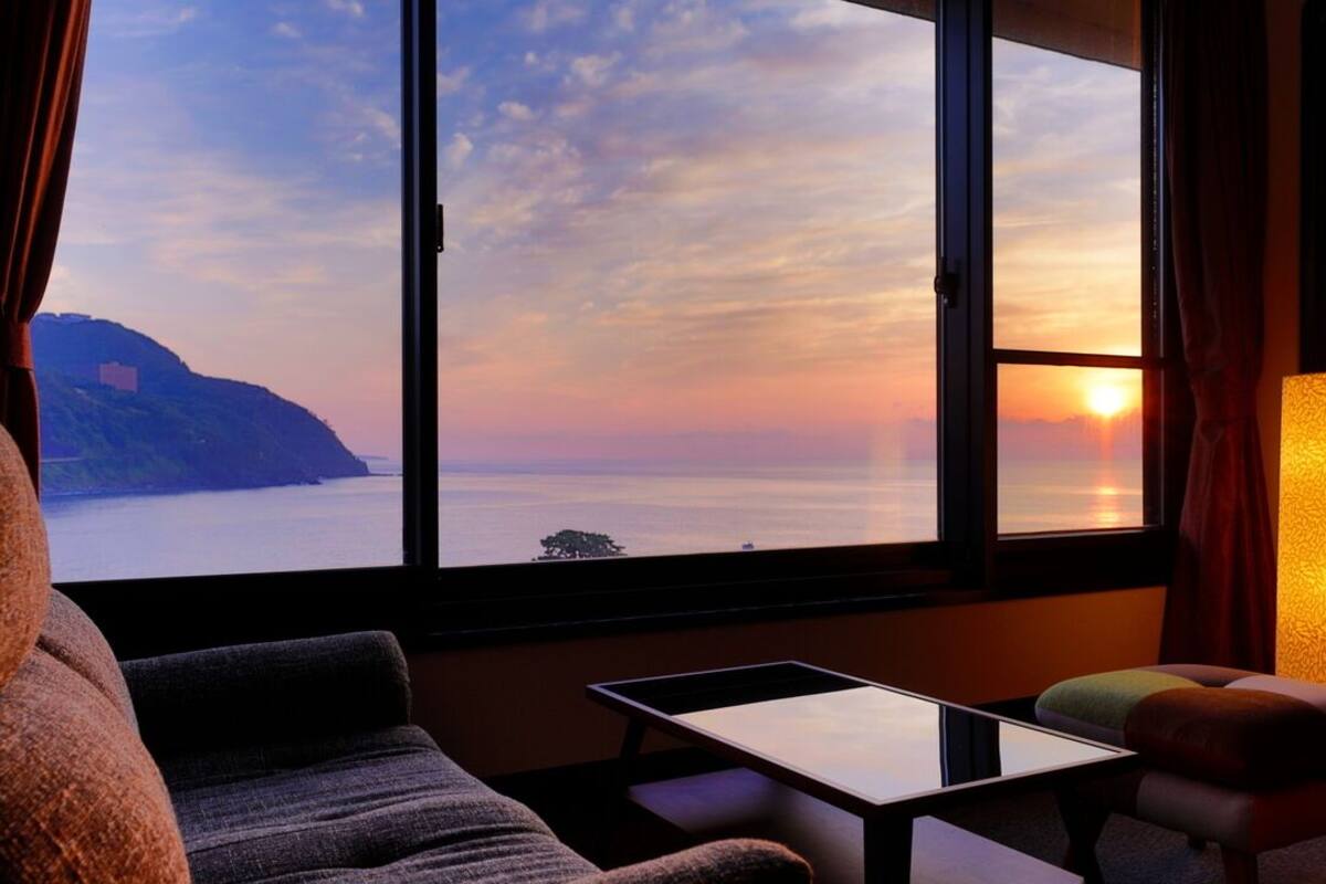 Um quarto com uma janela grande, um sofá, uma mesinha e um abajur.