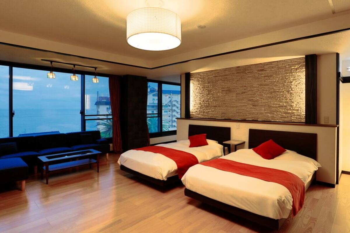 Quarto de hotel moderno com duas camas, um sofá, uma janela ampla com vista e uma peça de arte original na parede.