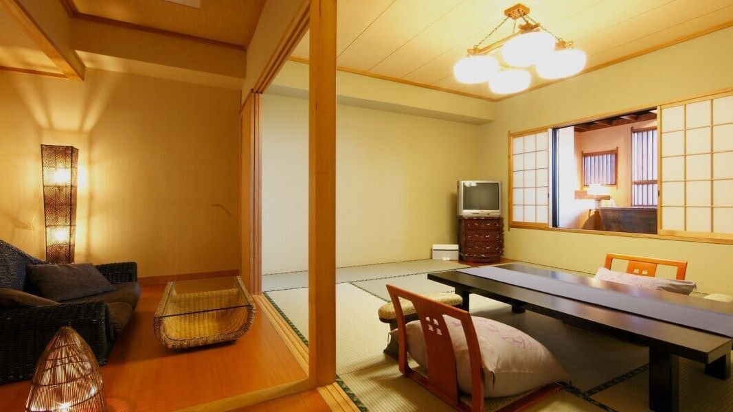 Um quarto japonês tradicional com tatames, uma mesa baixa, um sofá e uma televisão.