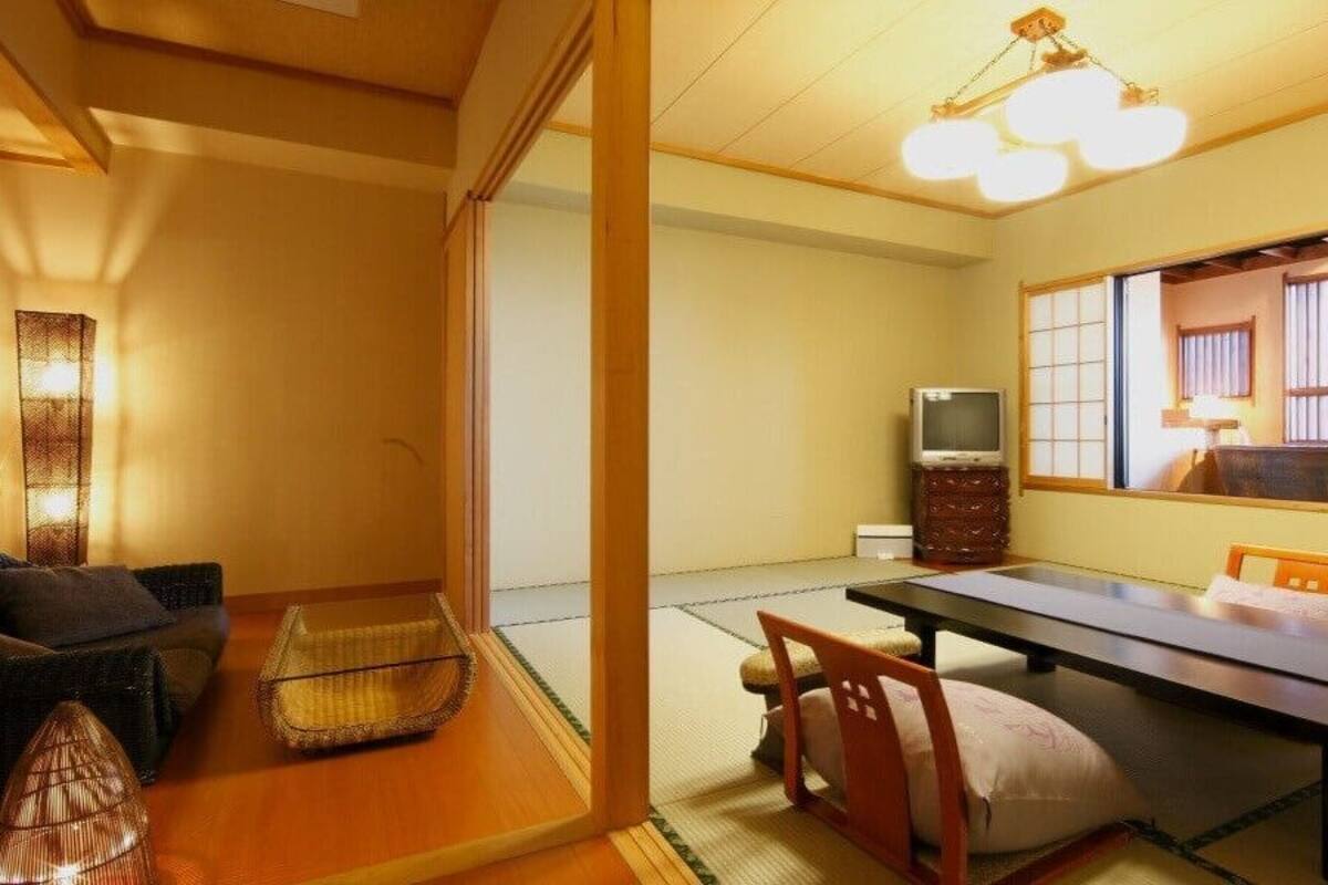 Um quarto japonês tradicional com tatames, uma mesa baixa, um sofá e uma televisão.