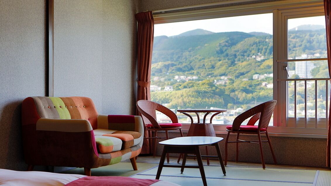 Quarto com sofá, duas cadeiras, mesa pequena e janela com vista para uma paisagem montanhosa.