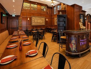 Restaurante com uma longa mesa de madeira posta para refeição, uma estátua de Buda e uma placa com a inscrição 'Bangkok Thai'.