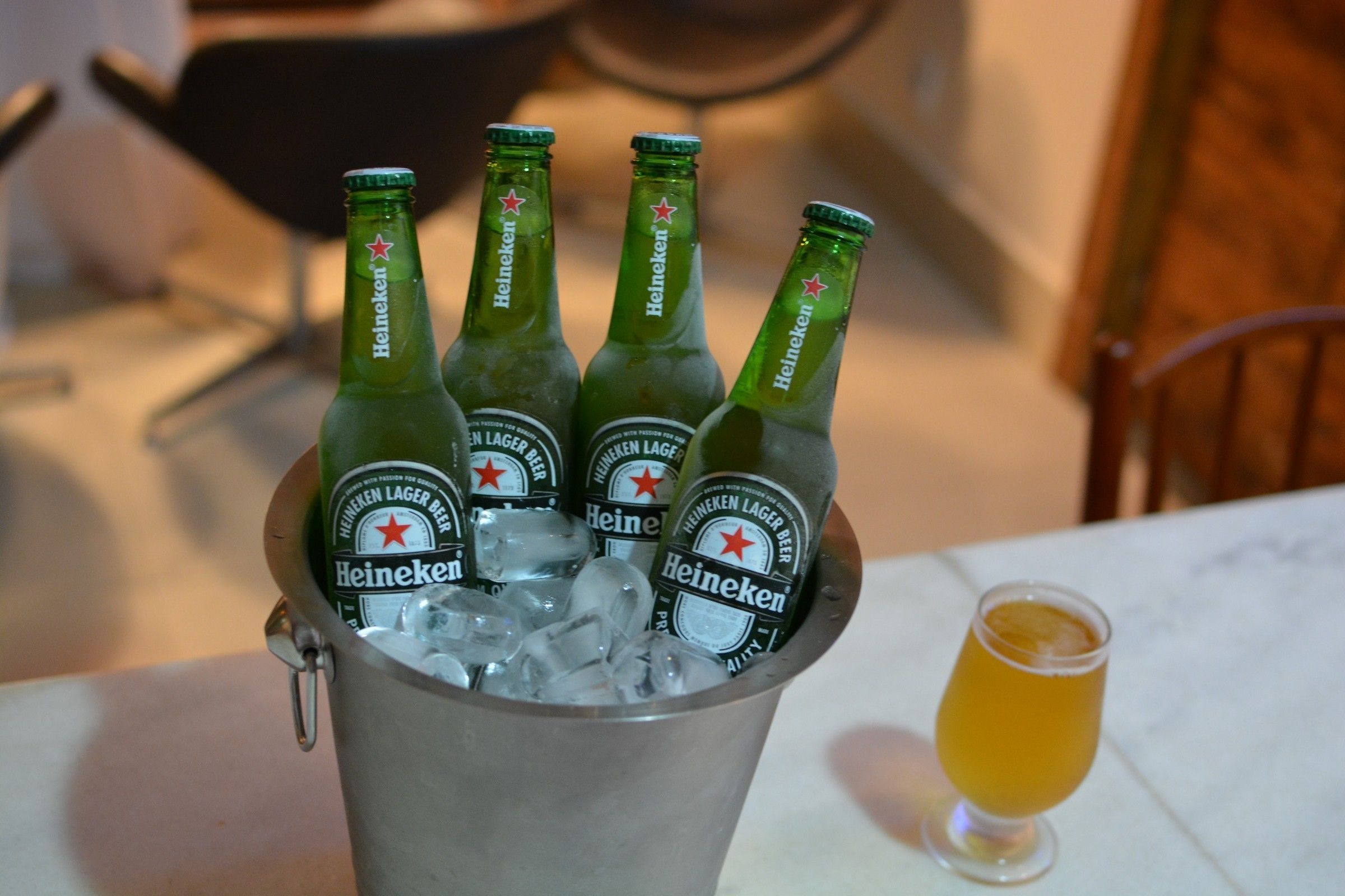 Um balde com quatro garrafas de cerveja Heineken e um copo de cerveja sobre uma mesa.