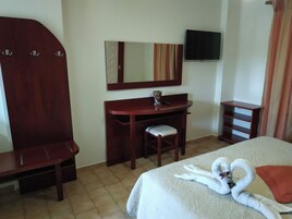 Quarto de hotel com cama, escrivaninha com cadeira, toucador, televisão e guarda-roupa.