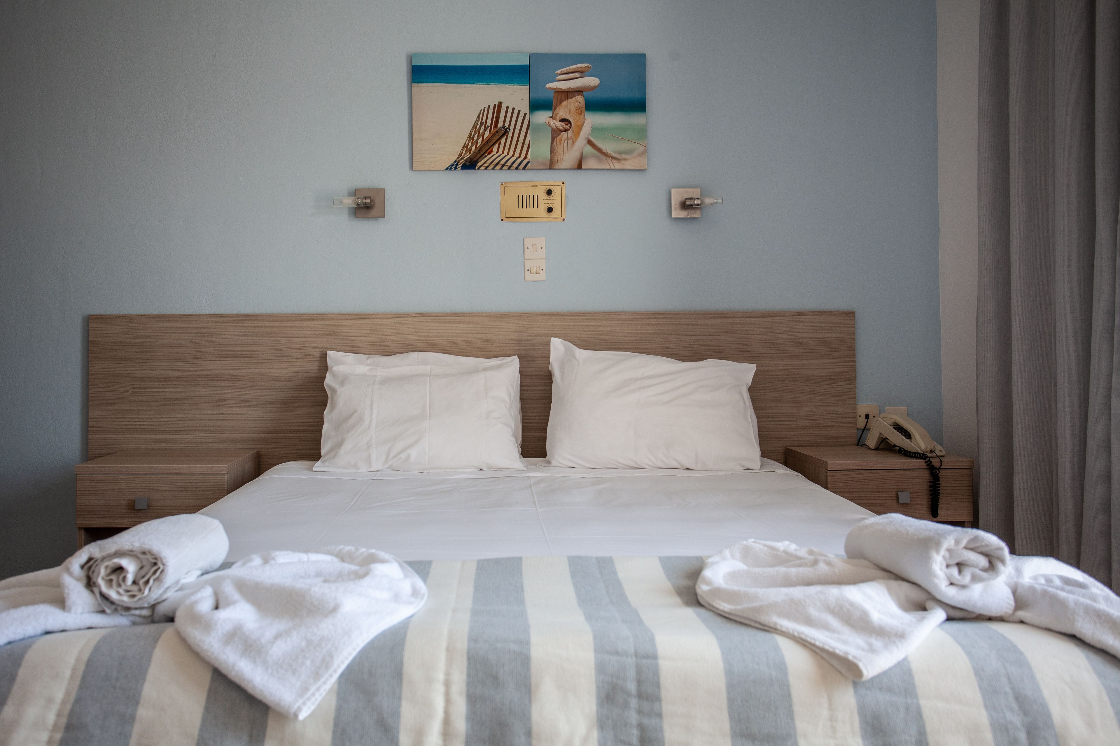 Cama bem arrumada com lençóis brancos e roupa de cama listrada, cabeceira de madeira e um quadro sobre a cama.