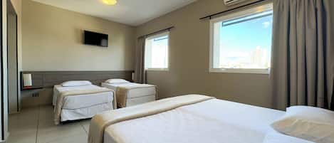 Quarto de hotel com três camas, televisão de tela plana na parede e janela com cortinas.