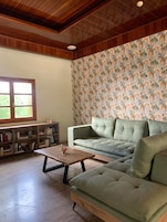 Uma sala de estar acolhedora com um sofá verde, uma mesa de centro de madeira e uma estante repleta de livros.