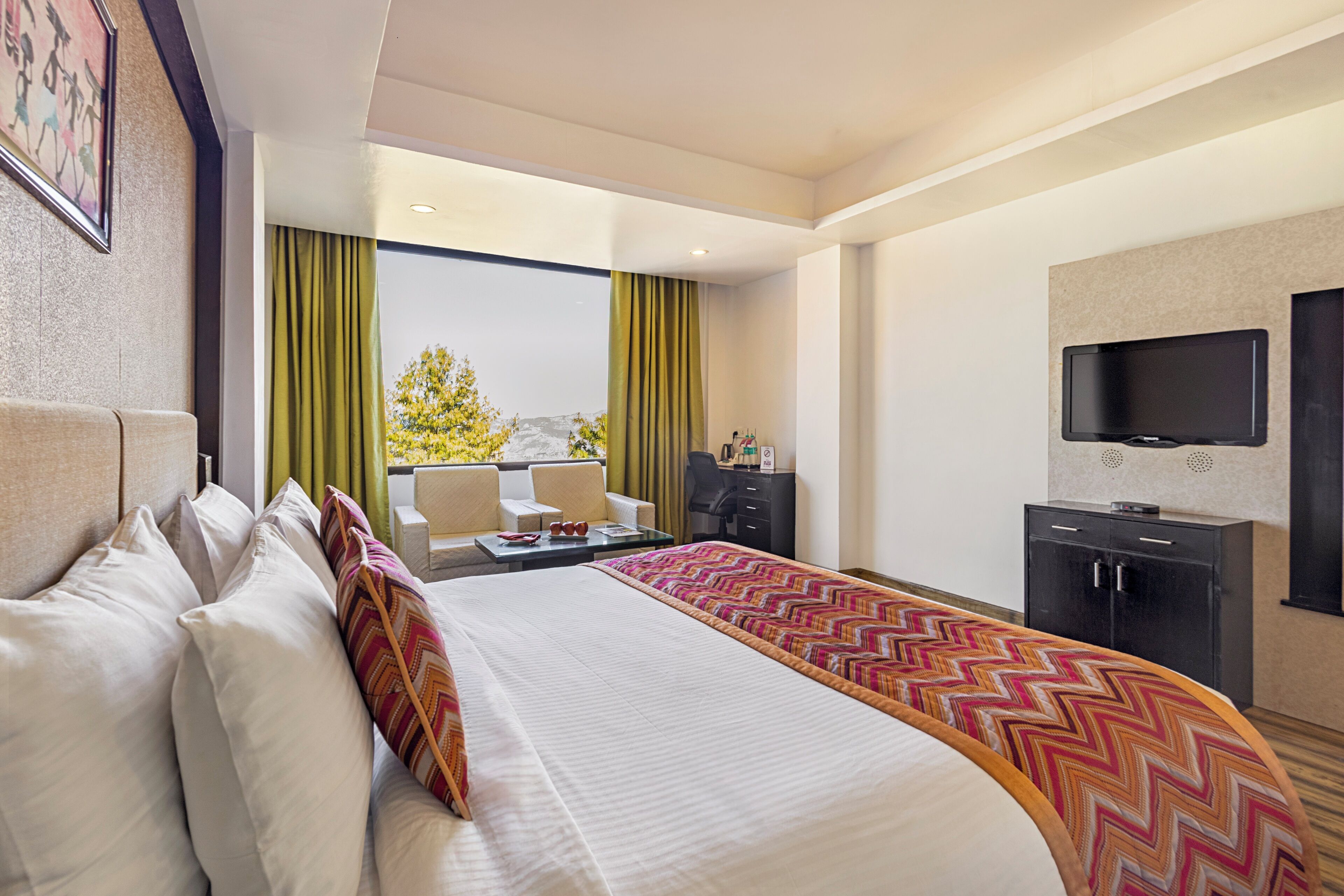 Quarto de hotel com uma cama grande, uma escrivaninha, uma cadeira, uma televisão e vista para o exterior.