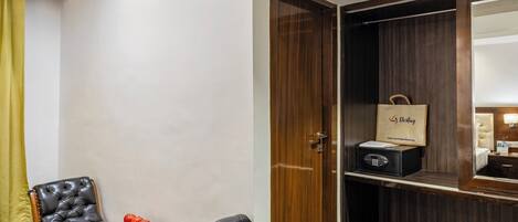 Quarto de hotel com piso de madeira, uma mesa de jantar com cadeiras, cama, guarda-roupa e espelho.