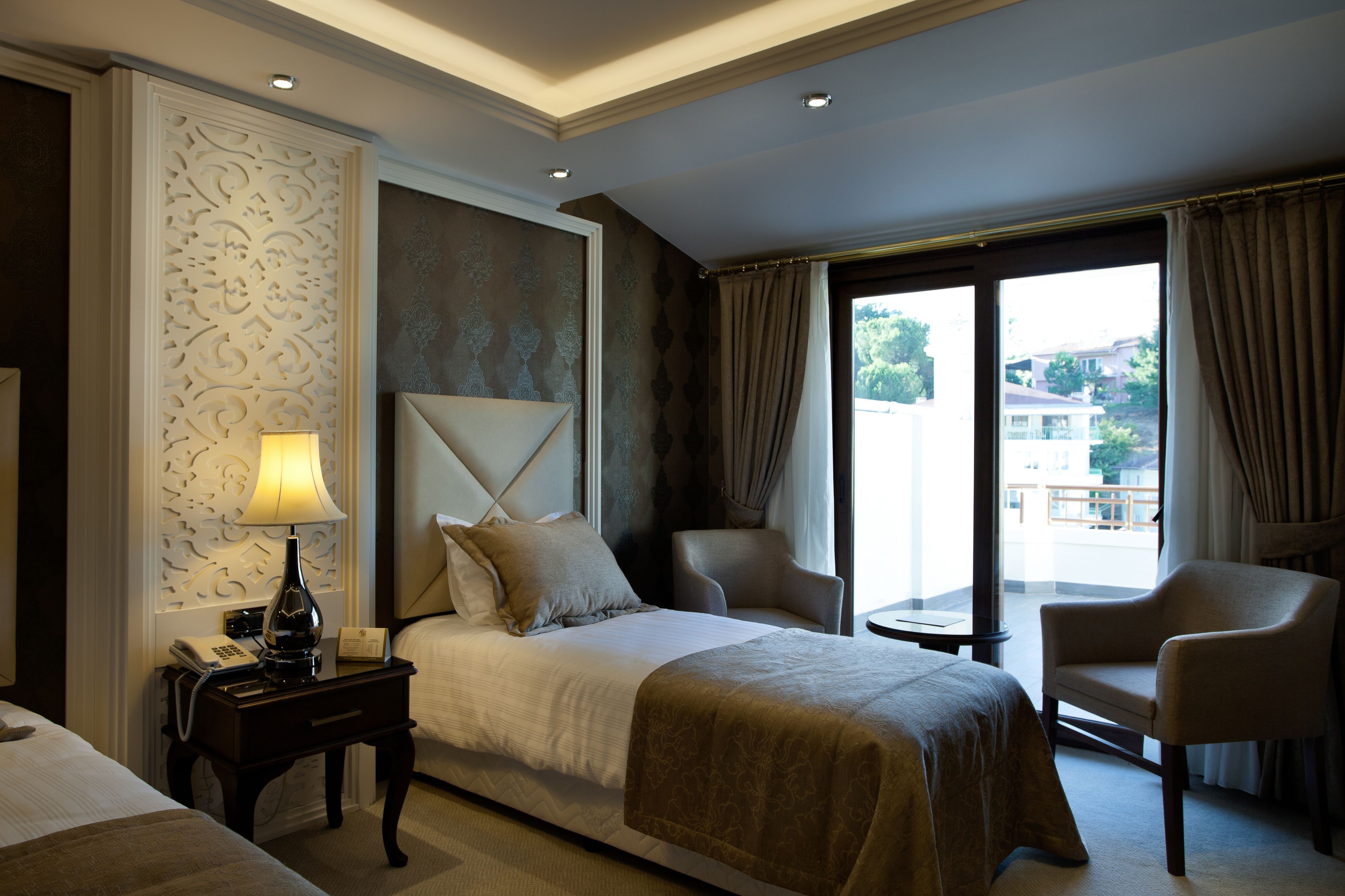 Quarto de hotel com uma cama grande, duas poltronas, uma mesa pequena e vista para o exterior.