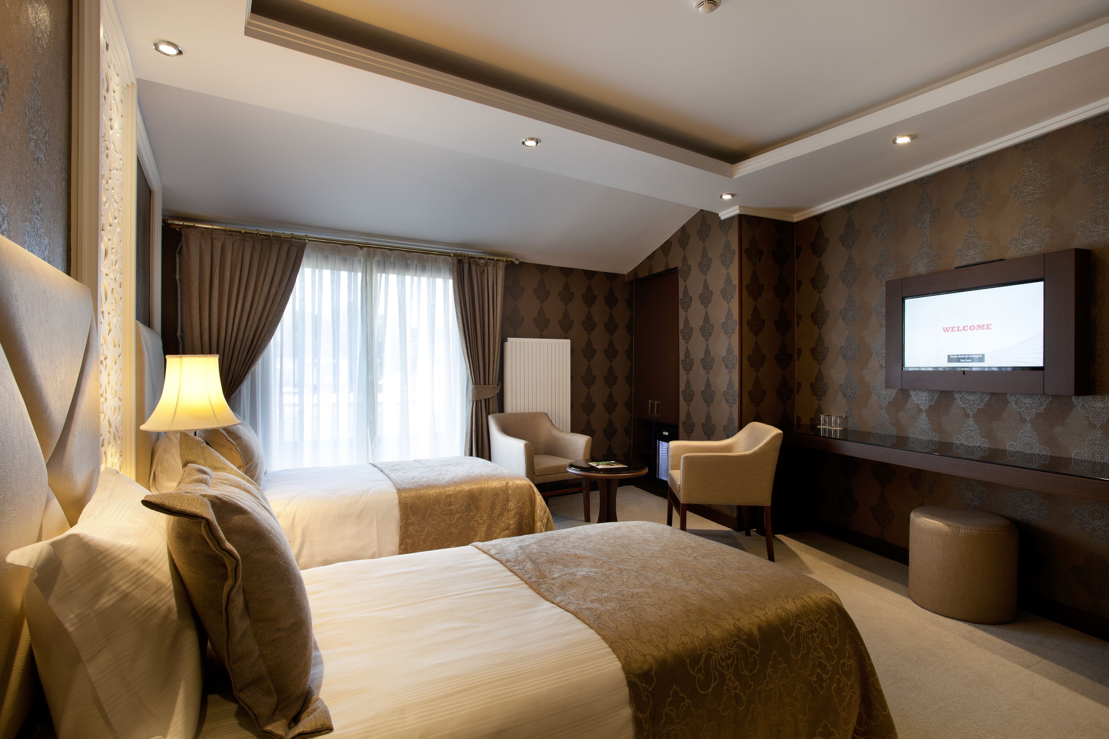 Quarto de hotel com duas camas, uma televisão, uma escrivaninha e uma cadeira.