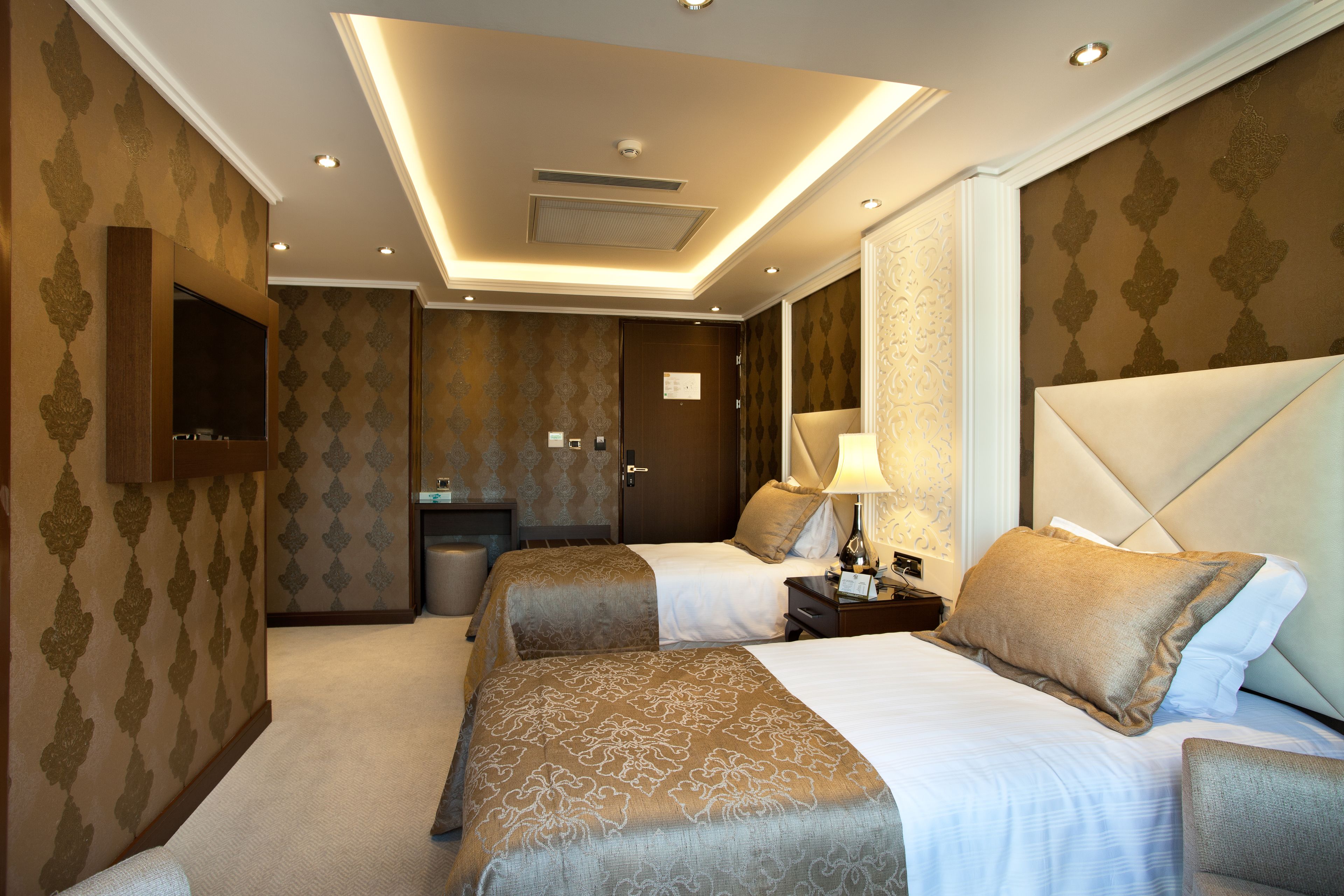 Quarto de hotel com duas camas, um espelho grande, mesa de cabeceira e televisão fixada na parede.