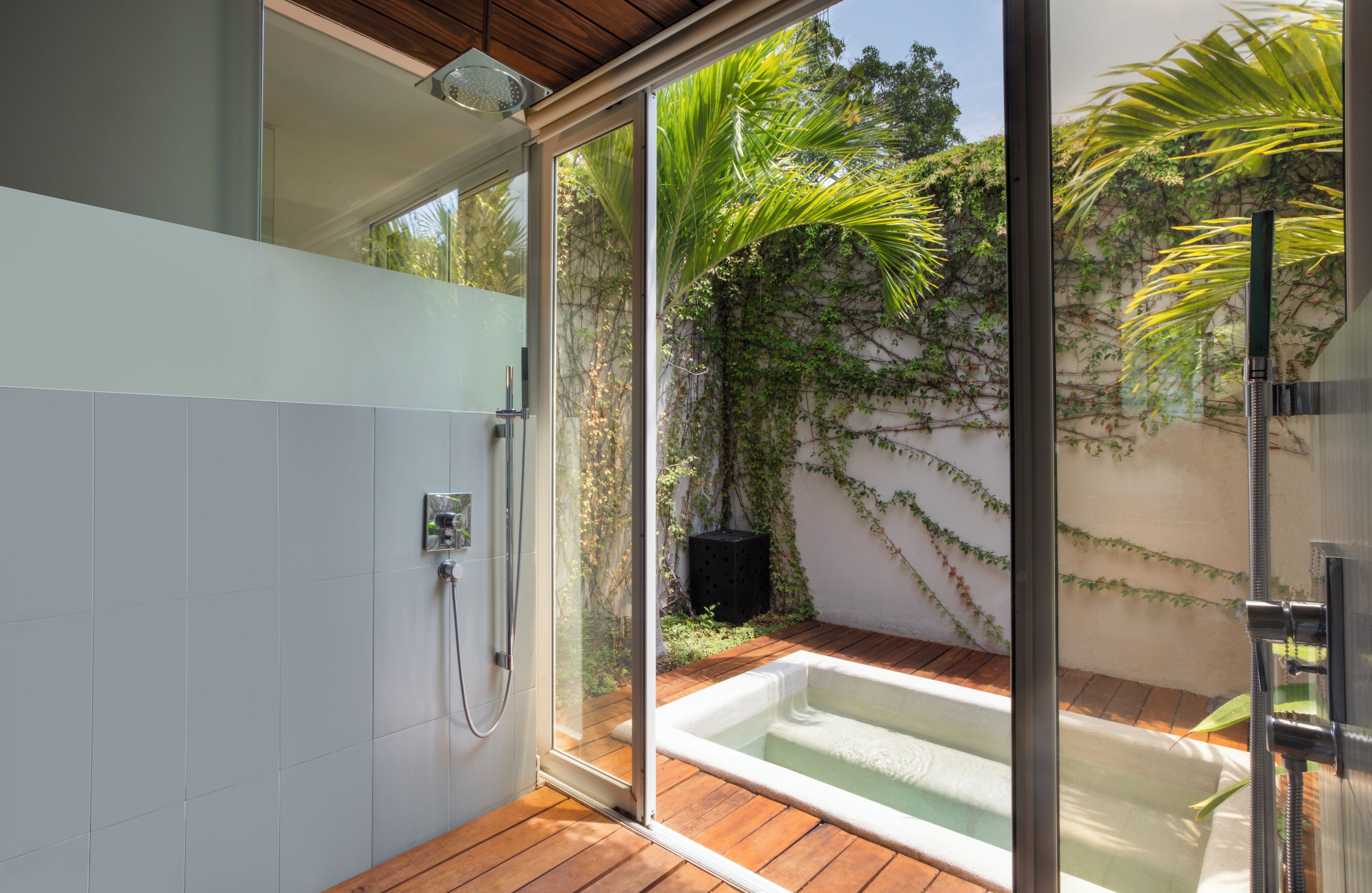 Casa de banho moderna com cabine de duche em vidro, soalho de madeira e uma pequena área de hidromassagem ao ar livre visível através das portas de vidro.