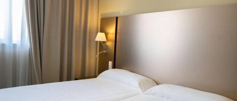 Quarto de hotel com cama, cortinas e luminária na parede.