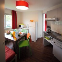 Uma cozinha compacta com mesa de jantar, cadeiras, geladeira, micro-ondas e pia.