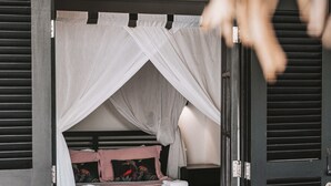 Quarto com cama sob dossel, uma cadeira e uma porta.