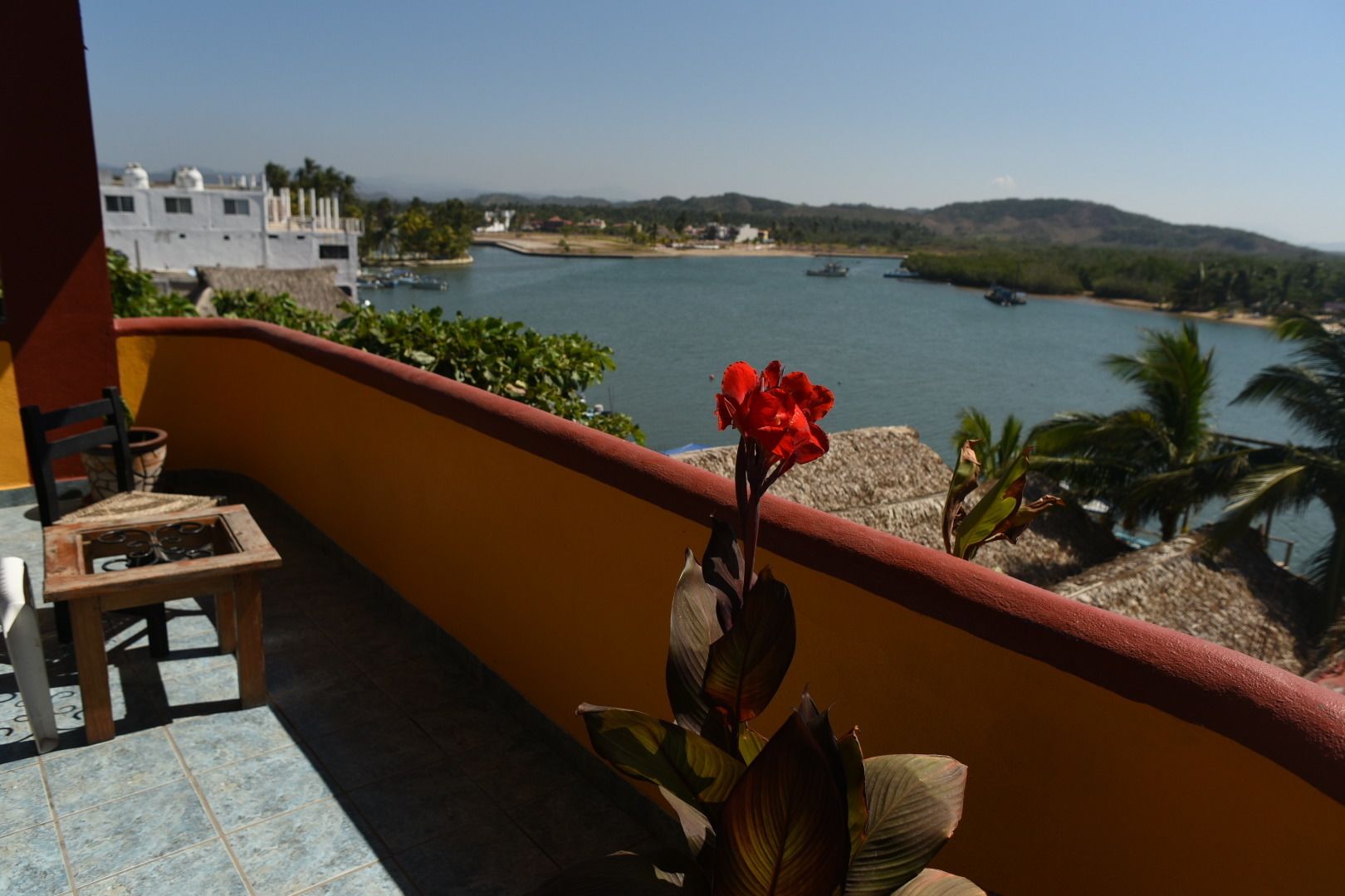 Uma varanda com vista para a água, uma cadeira, uma mesa e um vaso de planta.