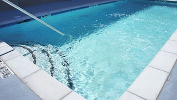 Piscina com água cristalina, prancha de mergulho e placa de proibição de mergulho.