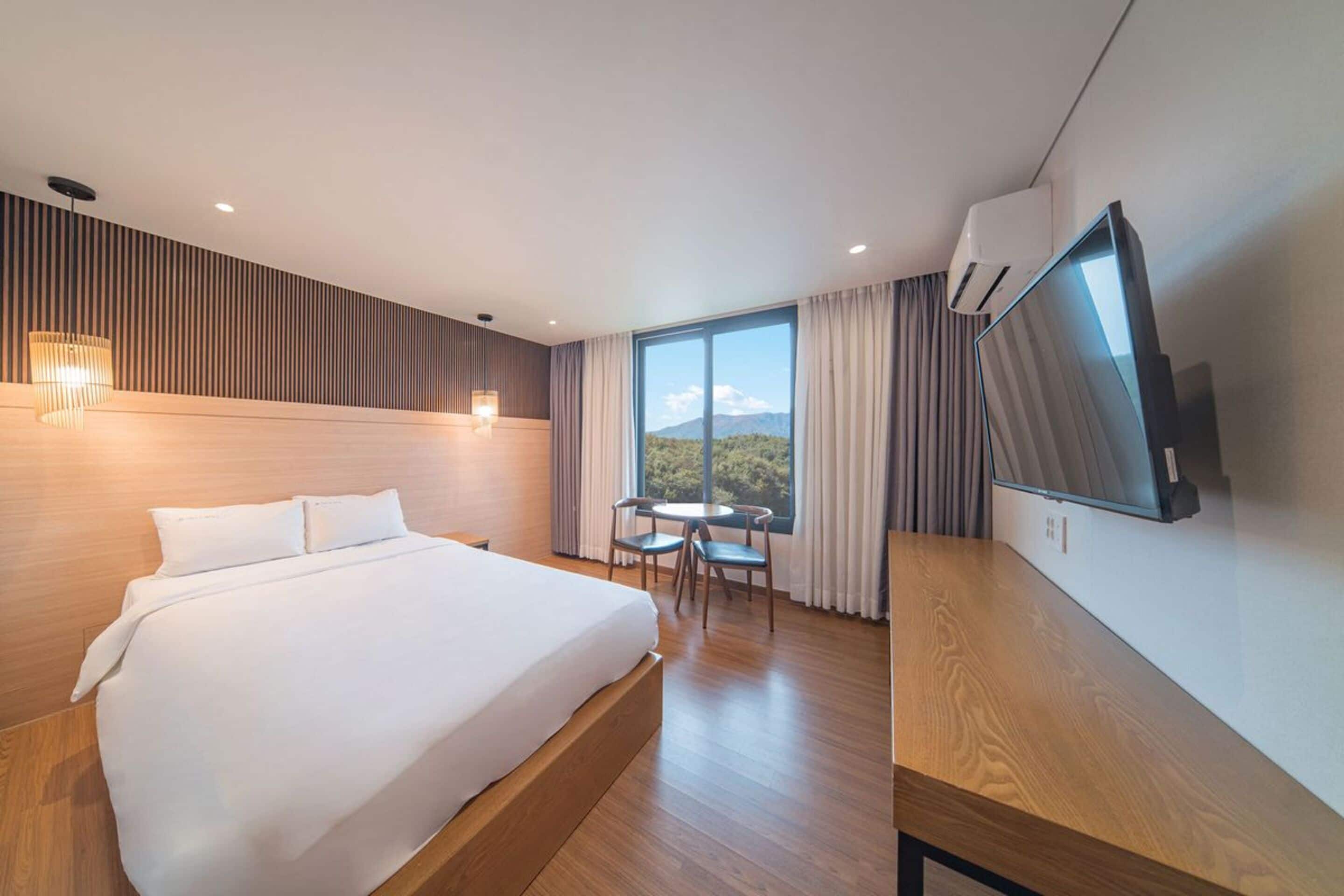 Quarto de hotel moderno com uma cama grande, uma mesa, uma televisão e vista para as montanhas.