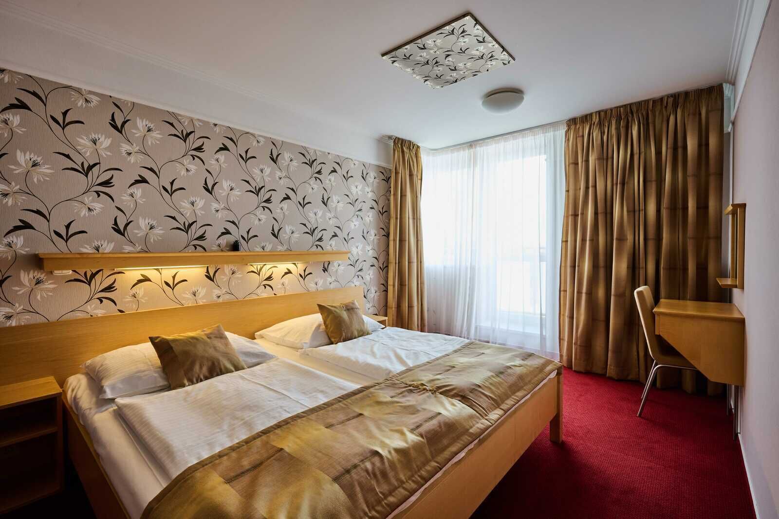 Quarto de hotel com uma cama grande, escrivaninha, cadeira, espelho e janela com cortinas.