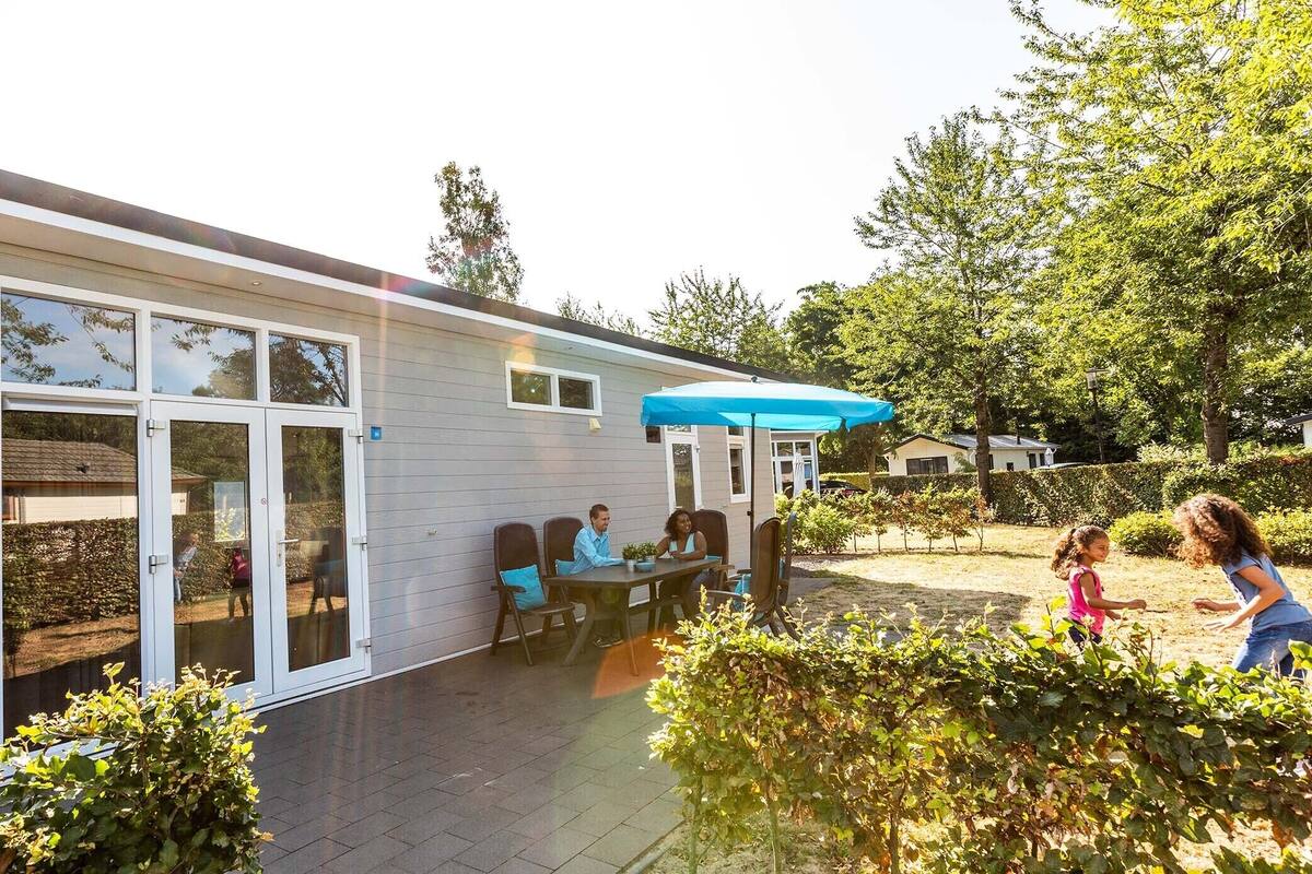 Uma casa moderna com um pátio, uma área de refeições com cadeiras e um guarda-sol azul.