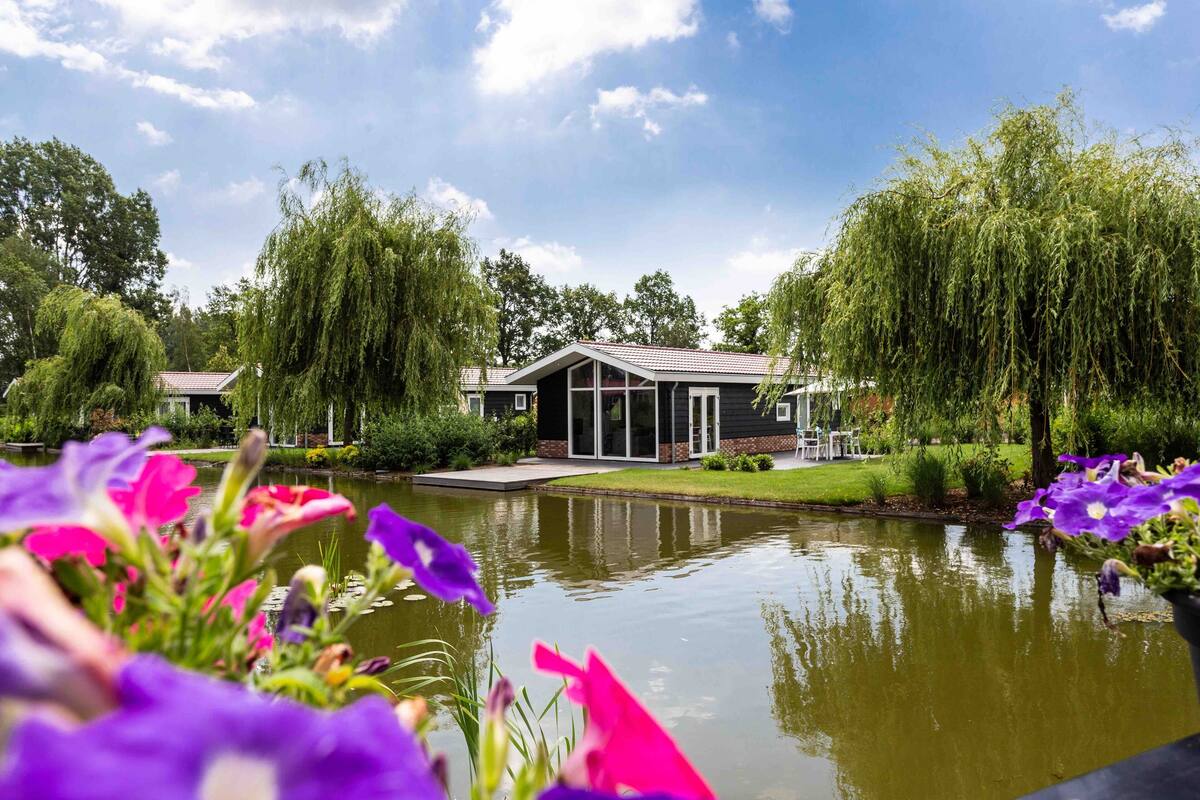 Um edifício moderno com fachada de vidro, rodeado por um lago e vegetação exuberante.