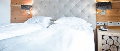 Quarto com cabeceira estofada, roupa de cama branca, mesa de cabeceira com telefone e luminária fixada na parede.