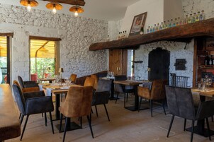 Interior de restaurante com paredes de pedra, vigas de madeira e diferentes opções de assentos.