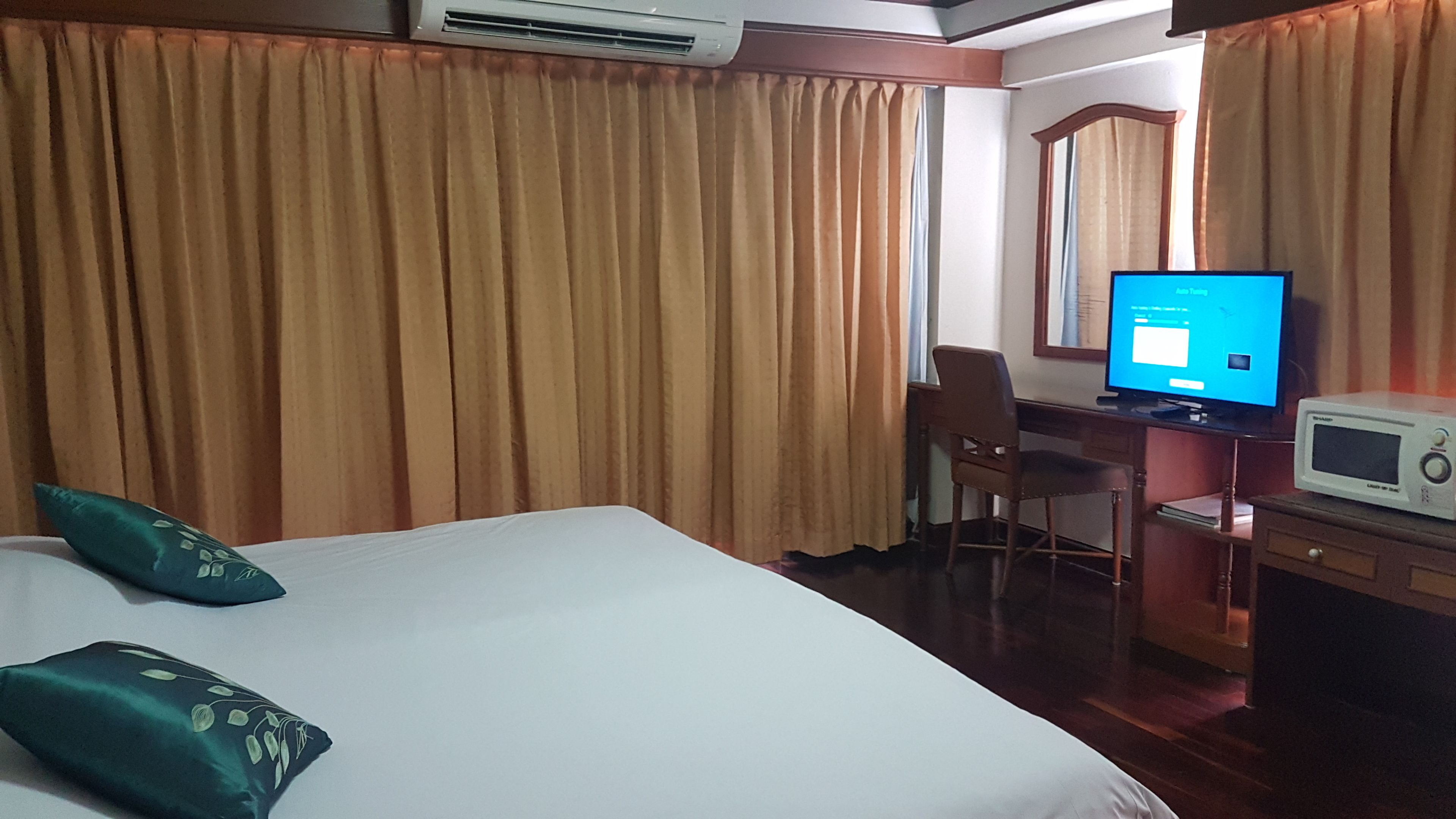 Quarto de hotel com cama, escrivaninha com computador, cadeira, micro-ondas e cortinas.