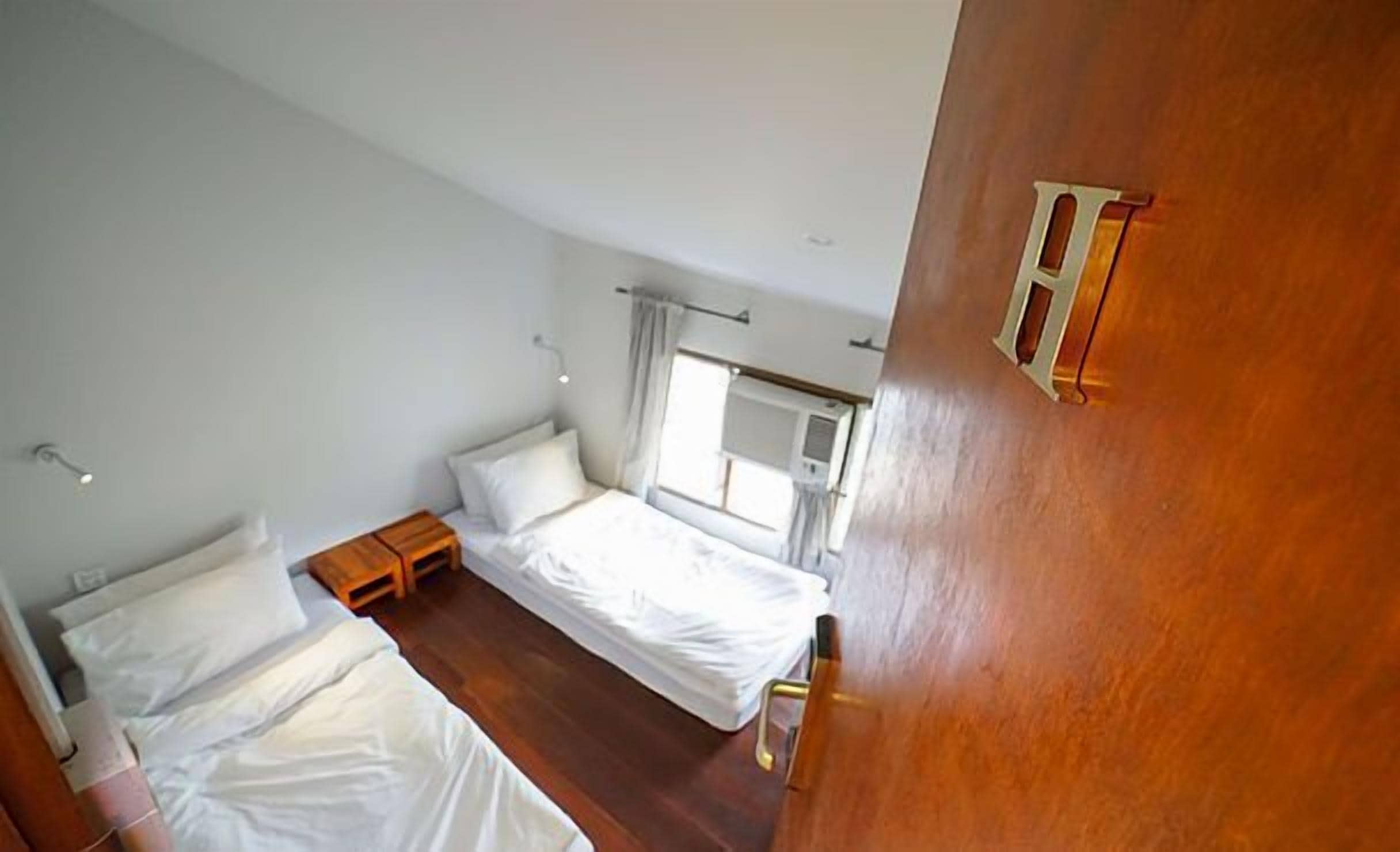 Quarto com duas camas, piso de madeira, janela com cortinas e ar condicionado fixado na parede.