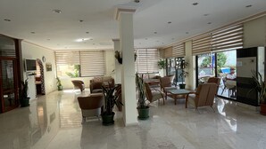 Um hall amplo com piso de mármore polido, áreas de estar confortáveis e grandes janelas com persianas.
