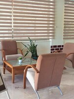 Um quarto com duas poltronas marrons, uma mesa de centro de vidro e um vaso com planta.