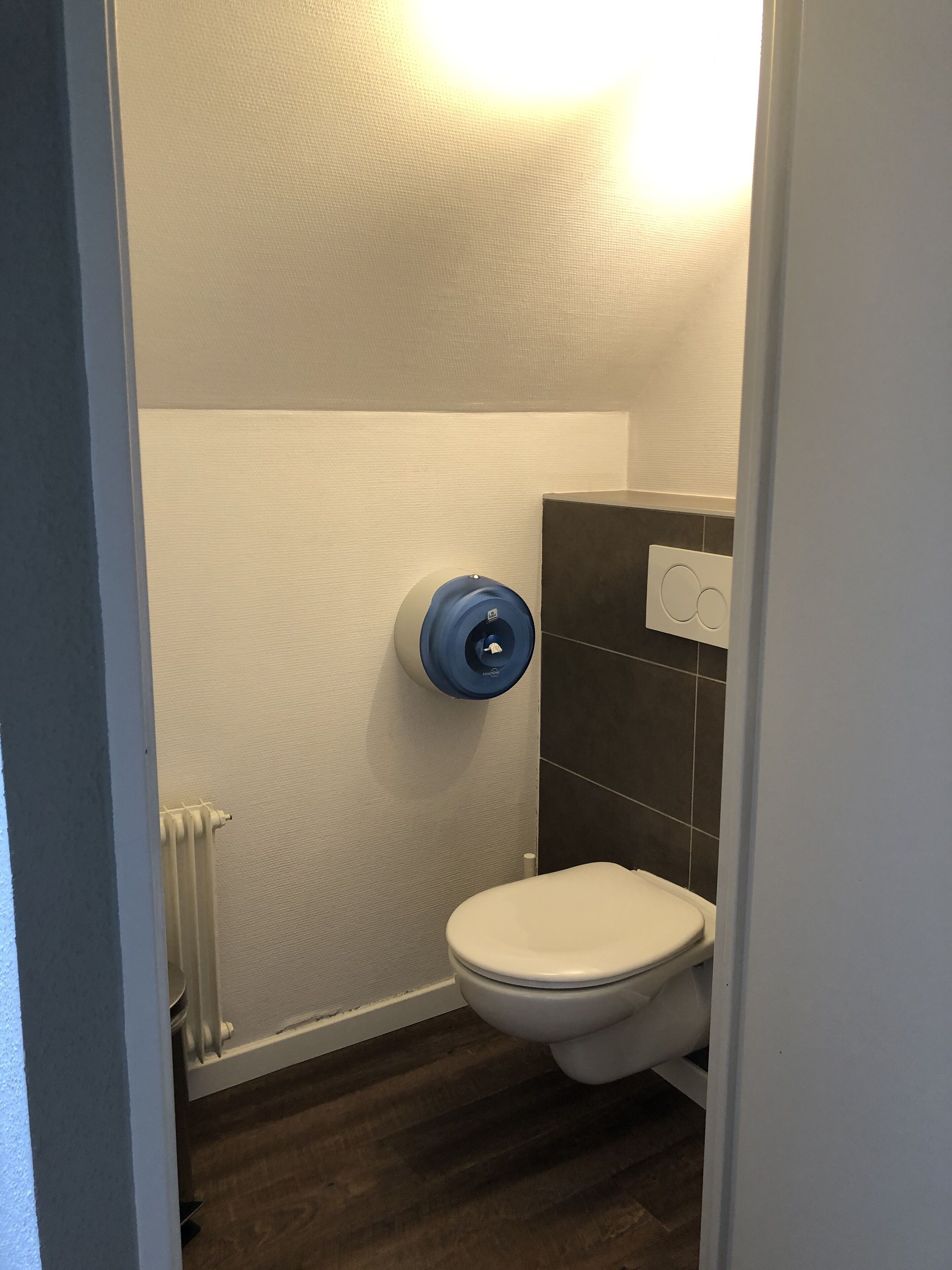 Um banheiro pequeno e moderno com vaso sanitário, secador de mãos e radiador.