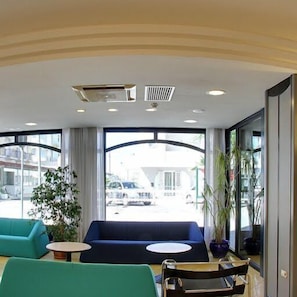 Um hall de hotel moderno com um sofá azul, uma mesa redonda e uma grande janela com vista para a rua.